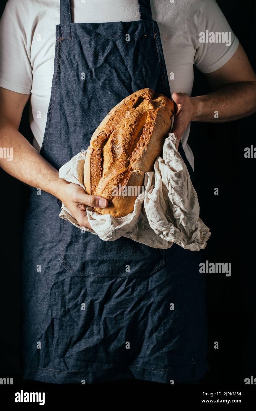 Crop unrecognizable male baker in apron demonstrating loaf of fresh ...
