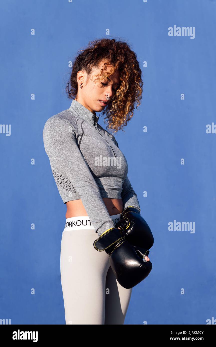 Side view of determined adult female boxer putting on boxing gloves ...