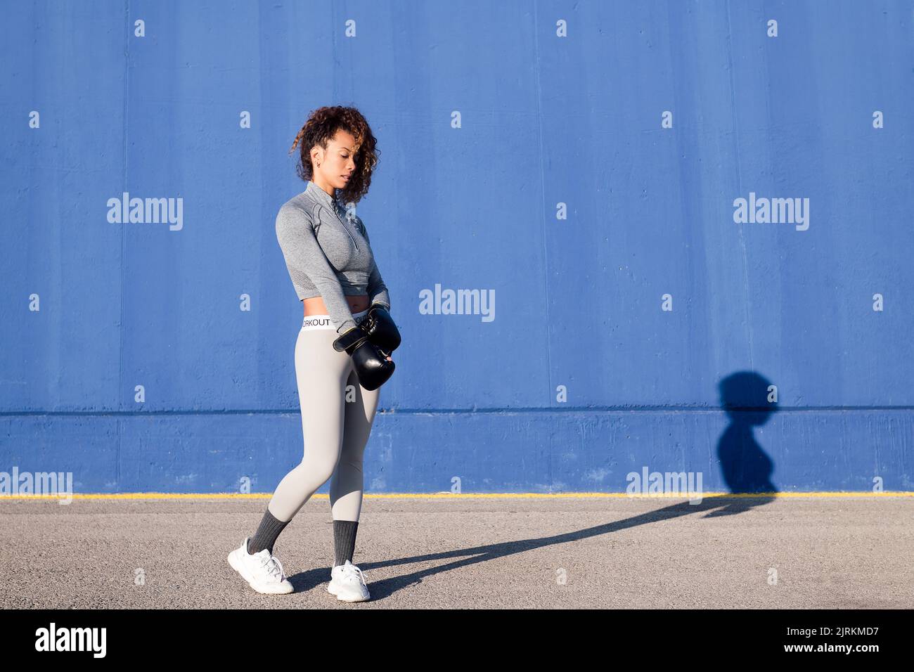 Side view of determined adult female boxer putting on boxing gloves ...