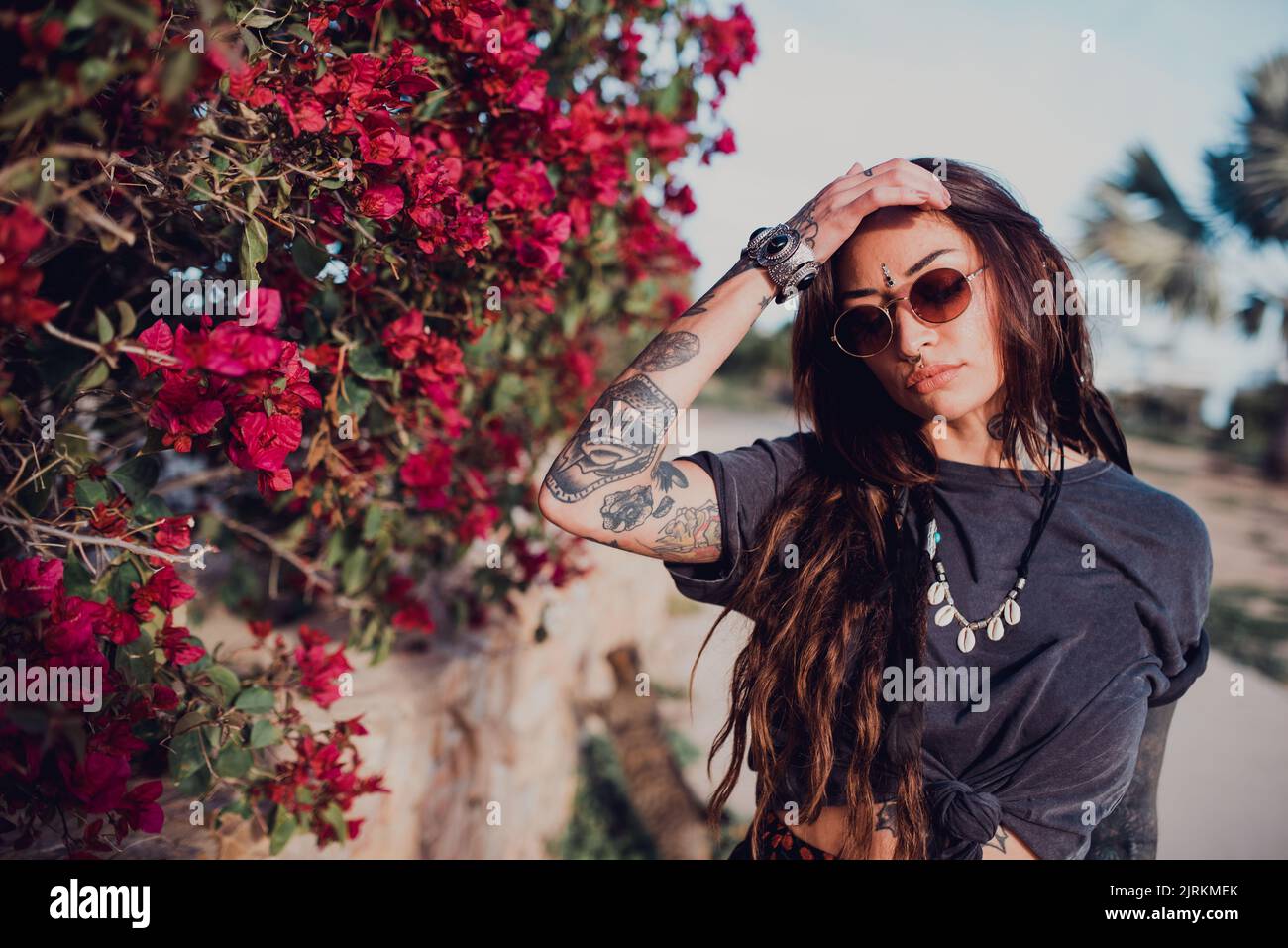 Confident stylish tattooed female with nose piercing and bindi touching ...