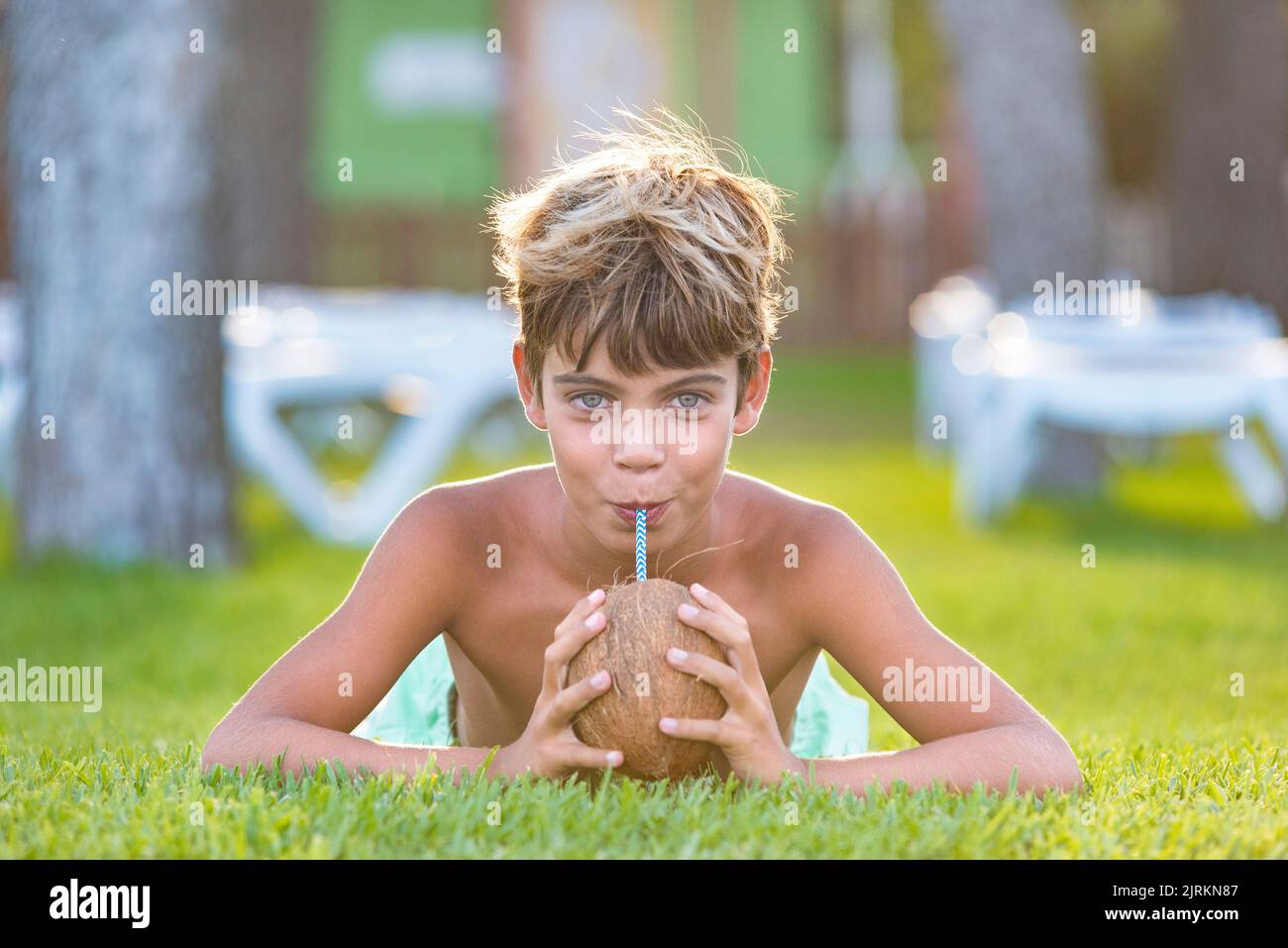 Carefree teenage boy lying on green lawn and drinking refreshing ...