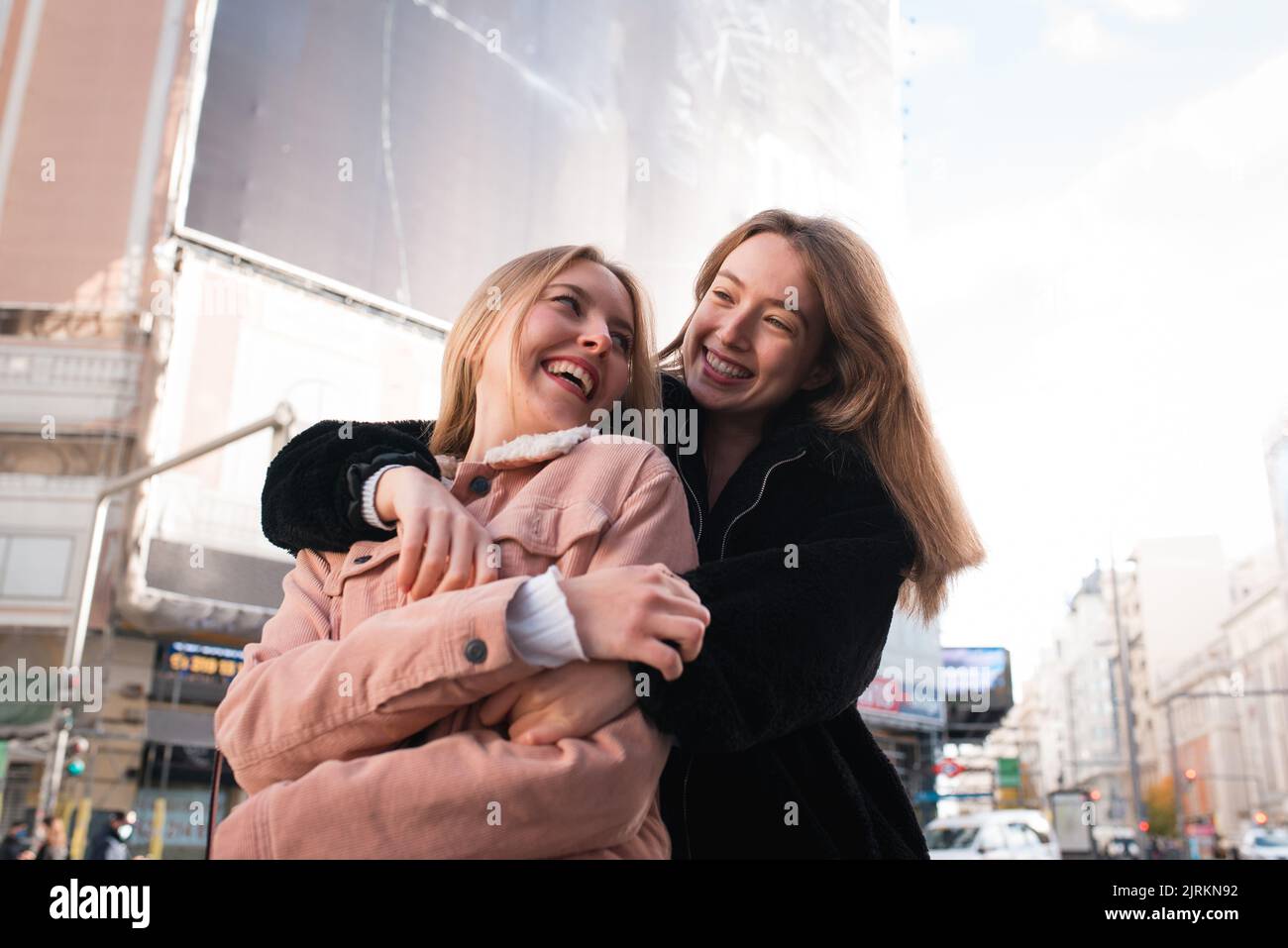 Low angle of smiling female best friends cuddling on street in Madrid ...