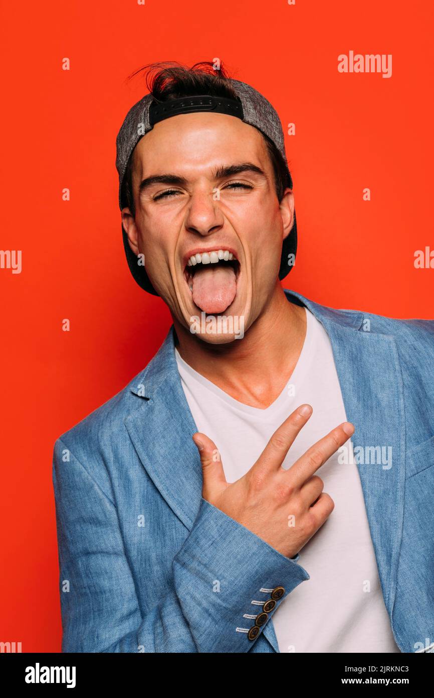 Young cool male in trendy wear and cap showing rap gesture while ...