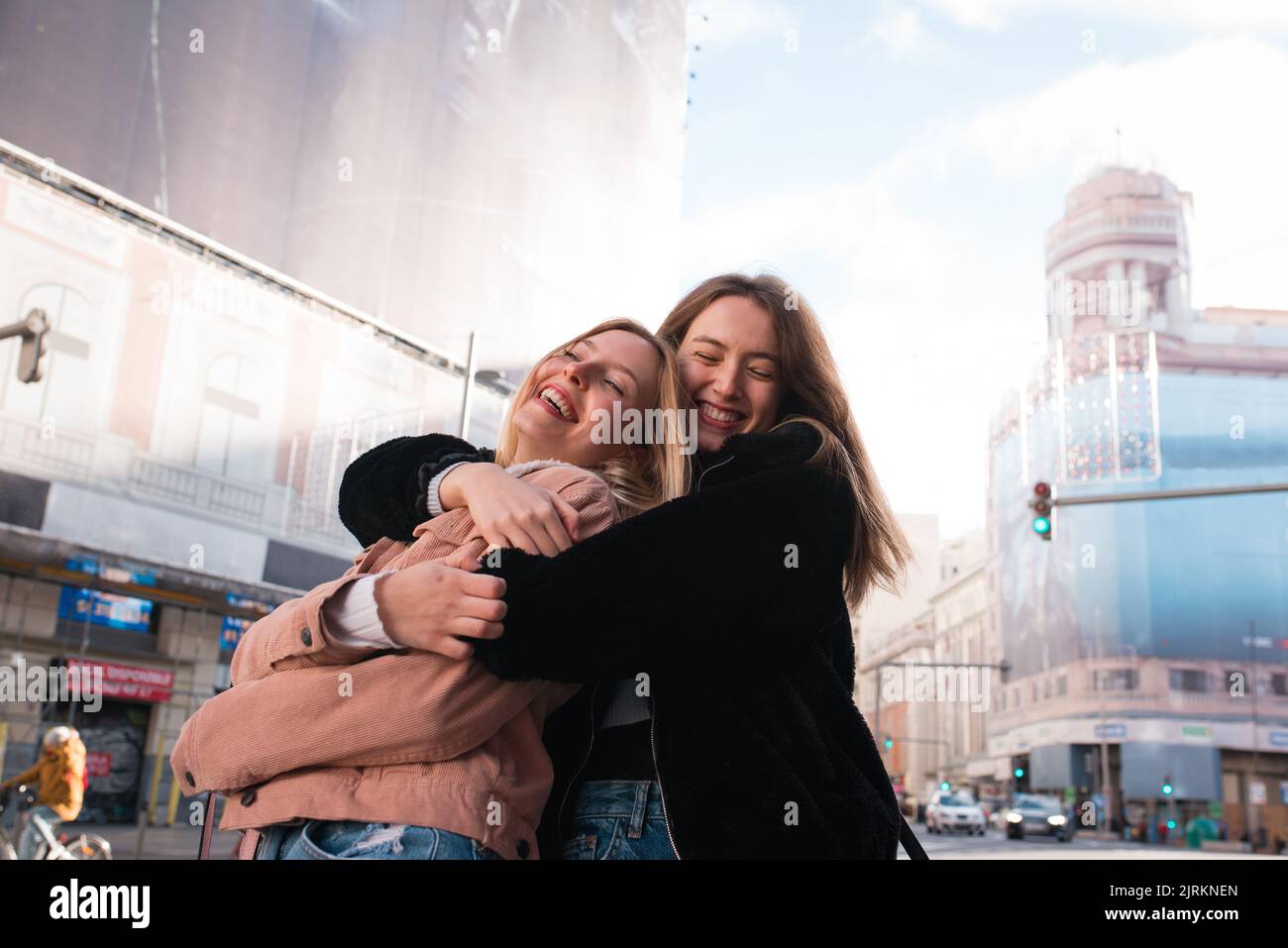 Low angle of smiling female best friends cuddling on street in Madrid ...