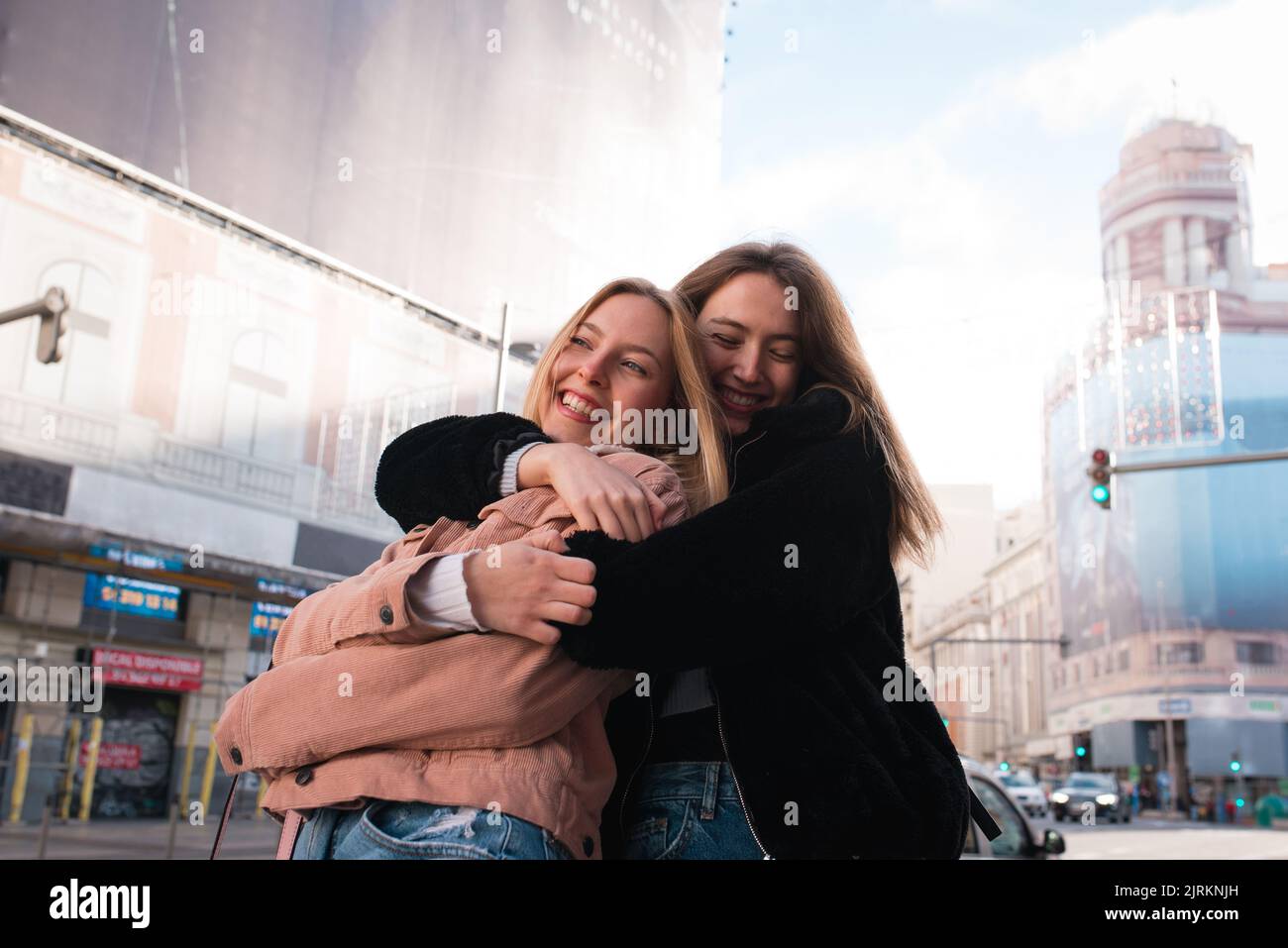 Low angle of smiling female best friends cuddling on street in Madrid ...