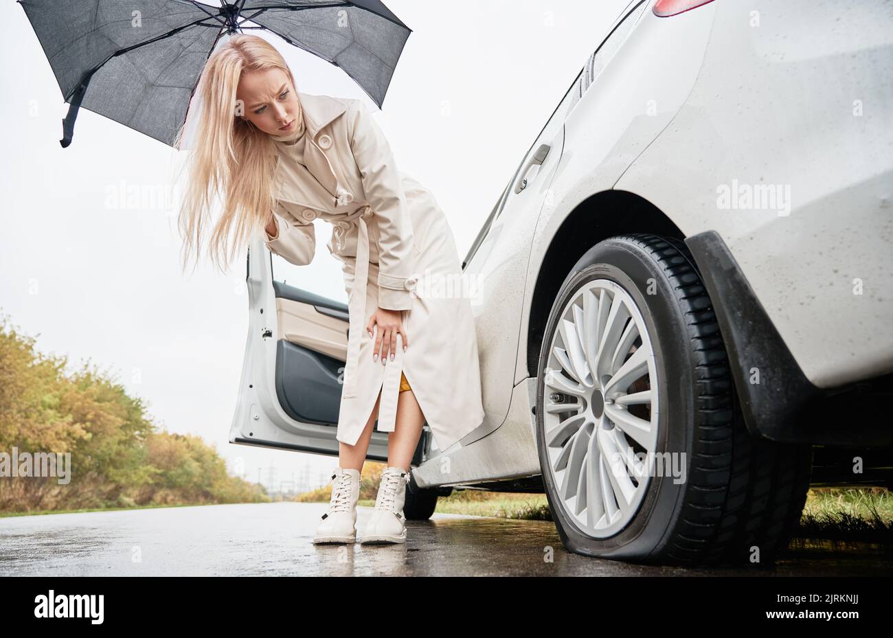 Beautiful woman on a road near her white car with punctured car tire ...