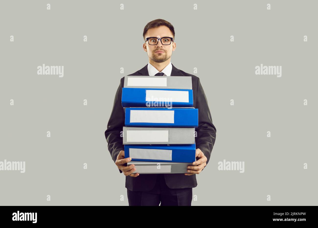 Tense male office worker with stressed expression holding stack of ...