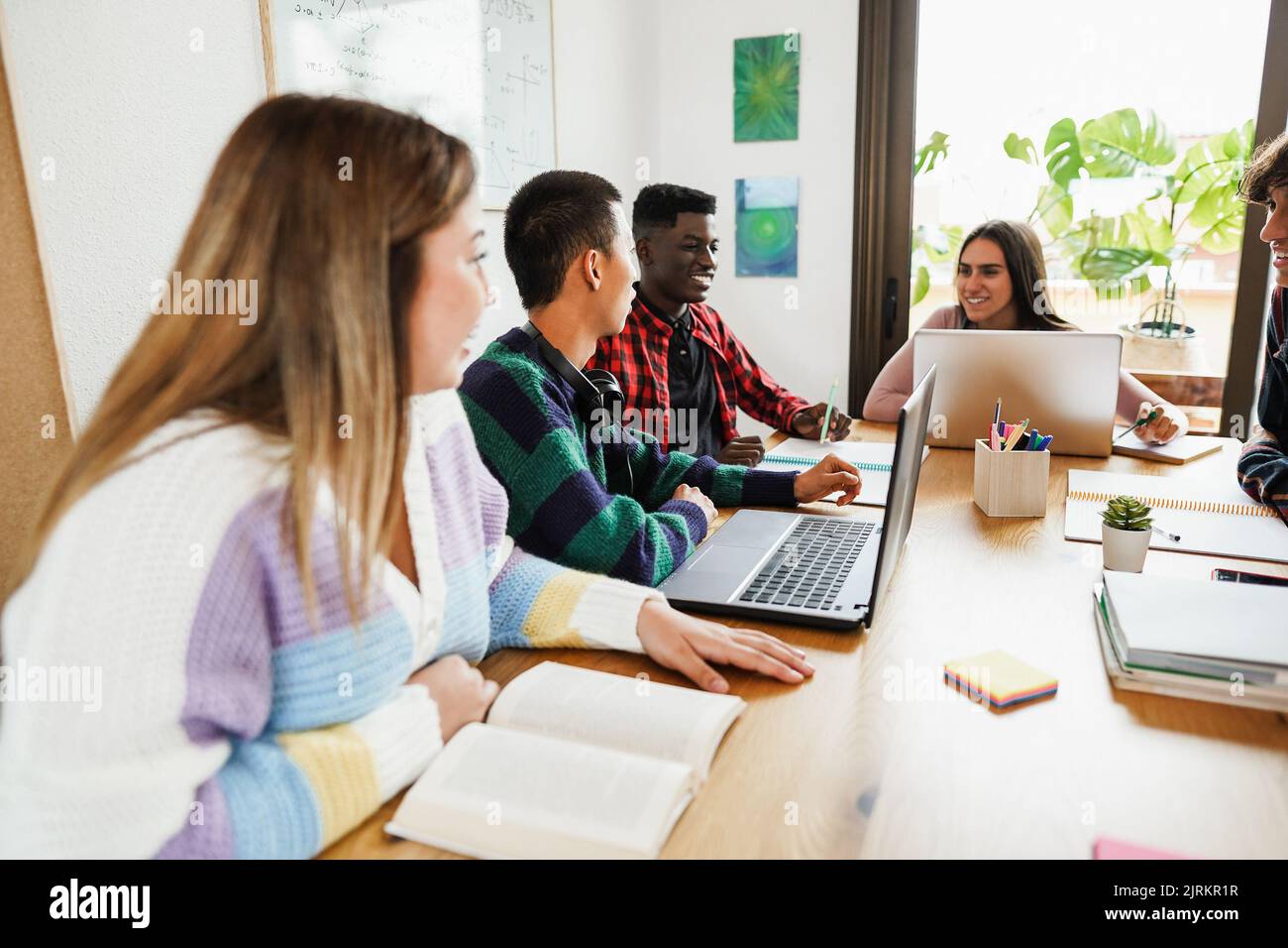 Multiracial students reading books and using laptop computers while studying at school library ...