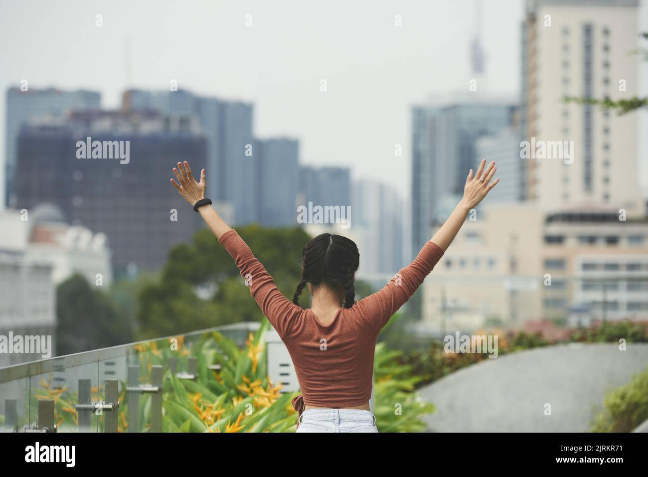 Rear view of happy young woman rising arms and looking at the city ...