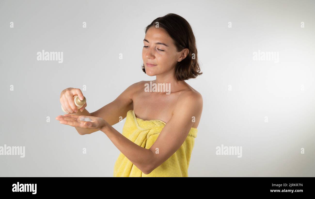 A woman squeezes the cream serum on the palm of her hand after a shower ...