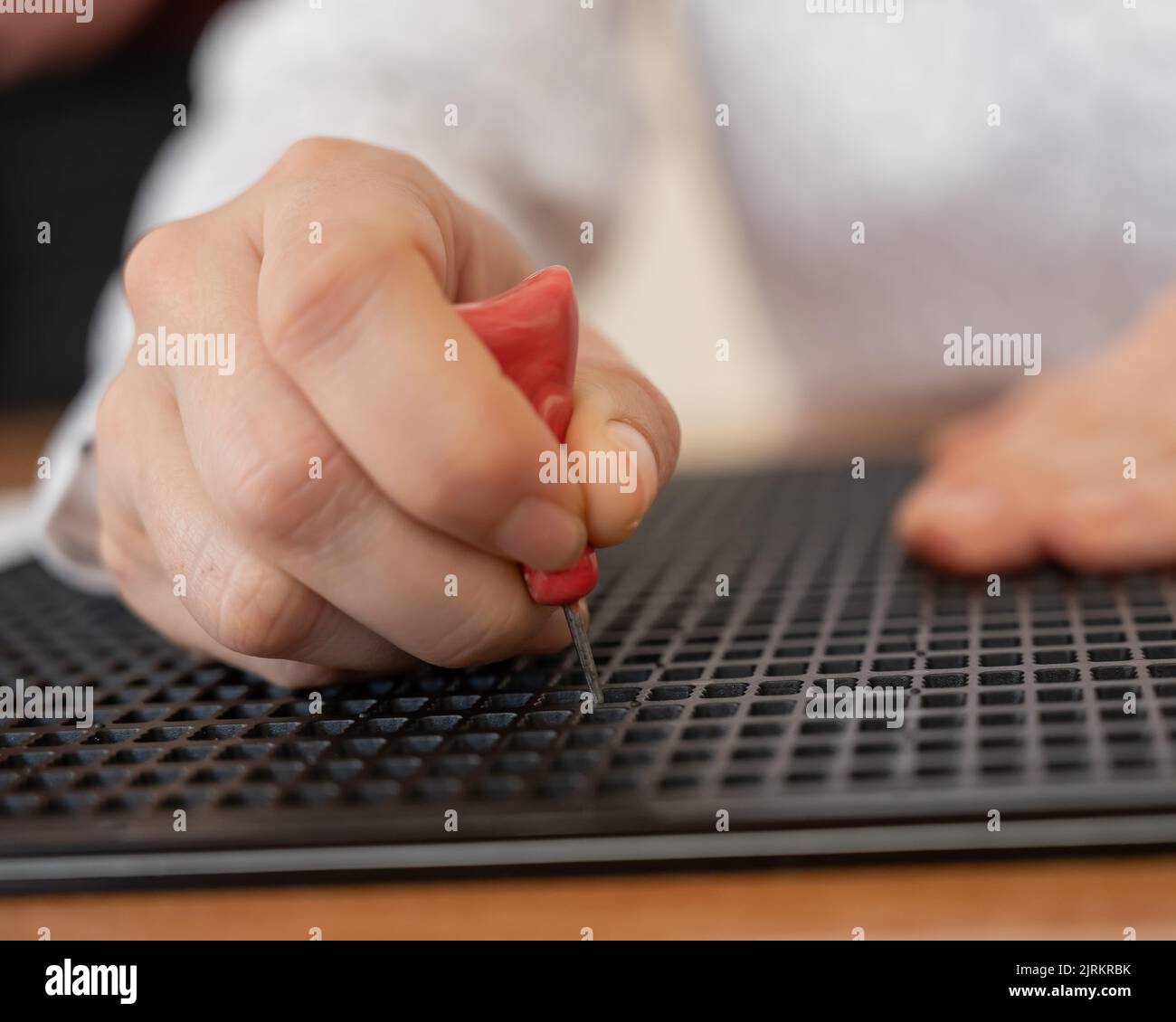 A woman uses a special stencil and stylus to write a letter in braille ...