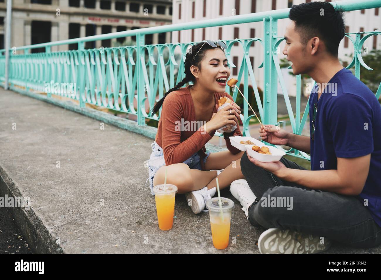 Asian couple sitting on pavement and eating street food Stock Photo - Alamy