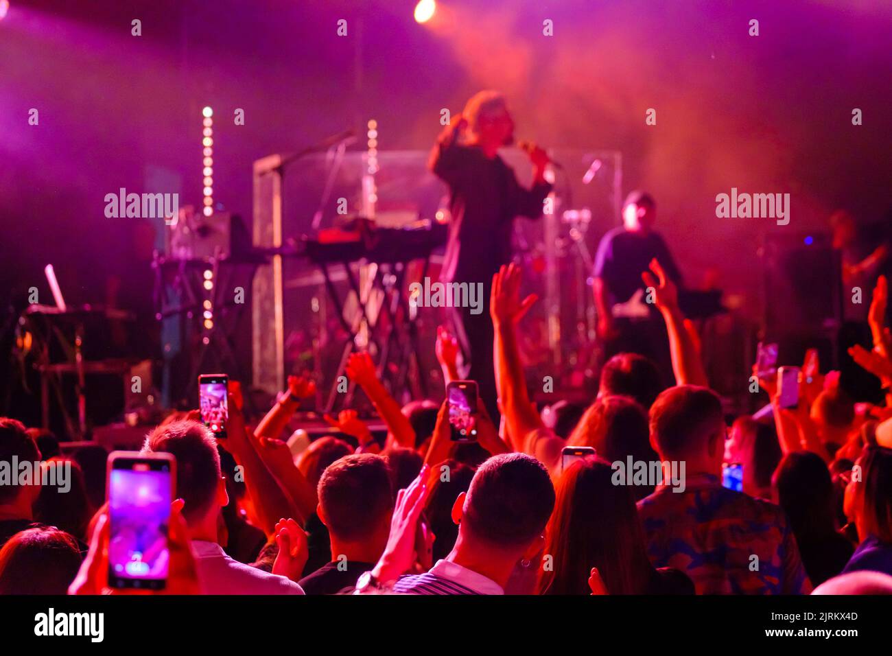 Anonymous people raising arms and dancing under red neon illumination ...