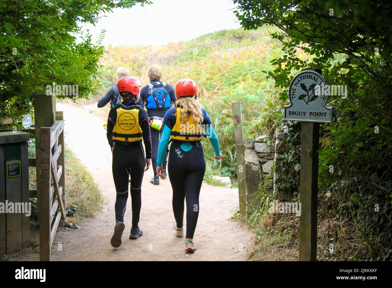 Coasteering group of people in wetsuits walking to coast at Baggy Point ...