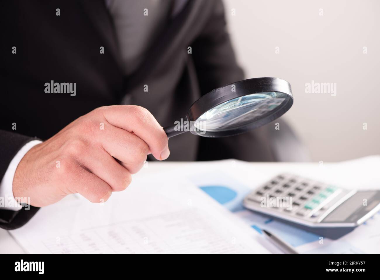Businessman examining document with magnifying glass sitting on desk ...