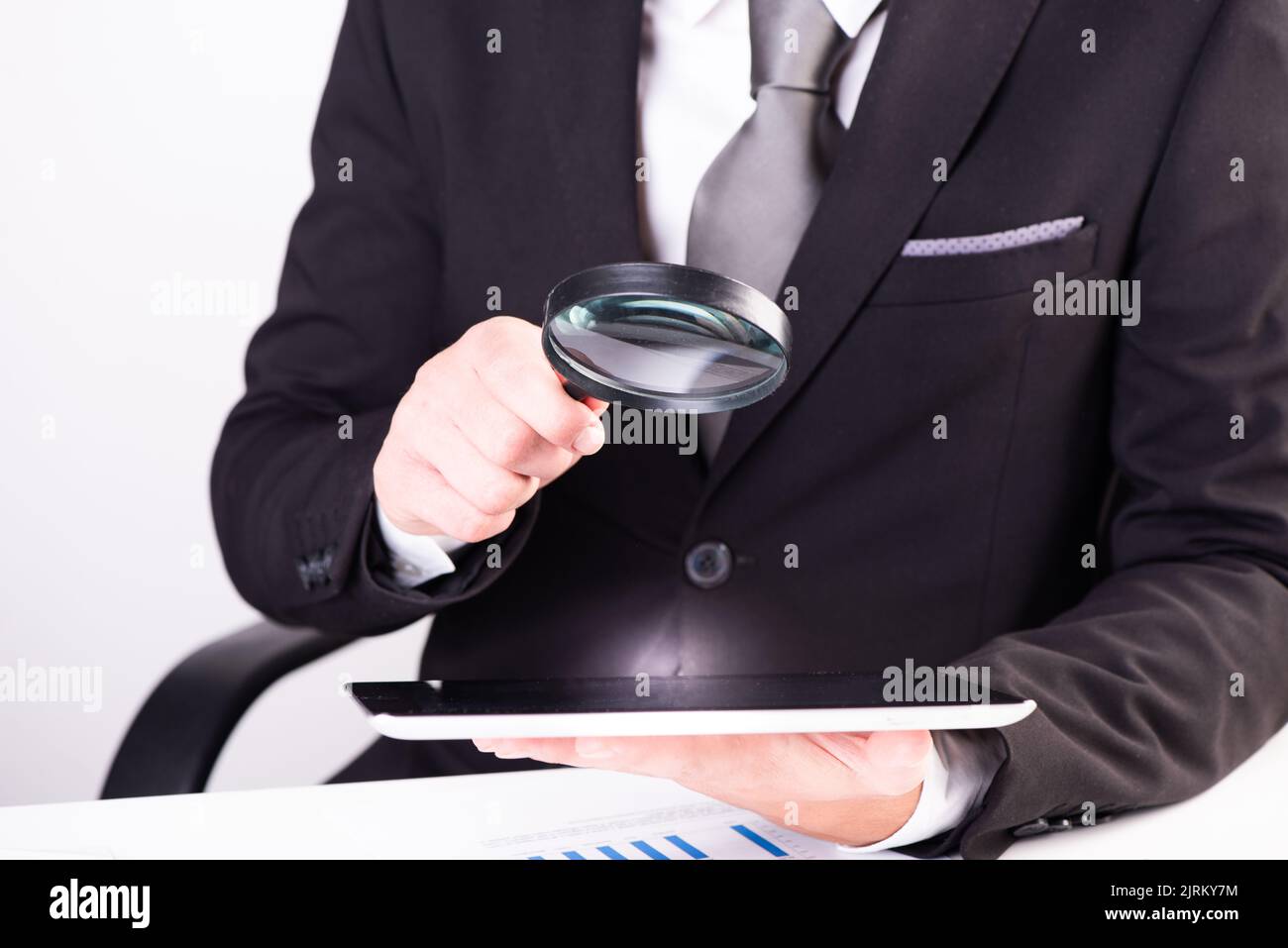 Auditor holding magnifying glass and tablet sitting on desk Stock Photo ...