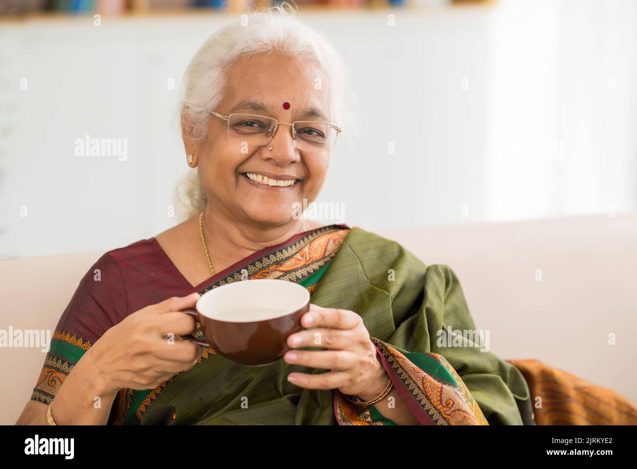 Happy elderly Indian woman in traditional dress having a cup of tea ...