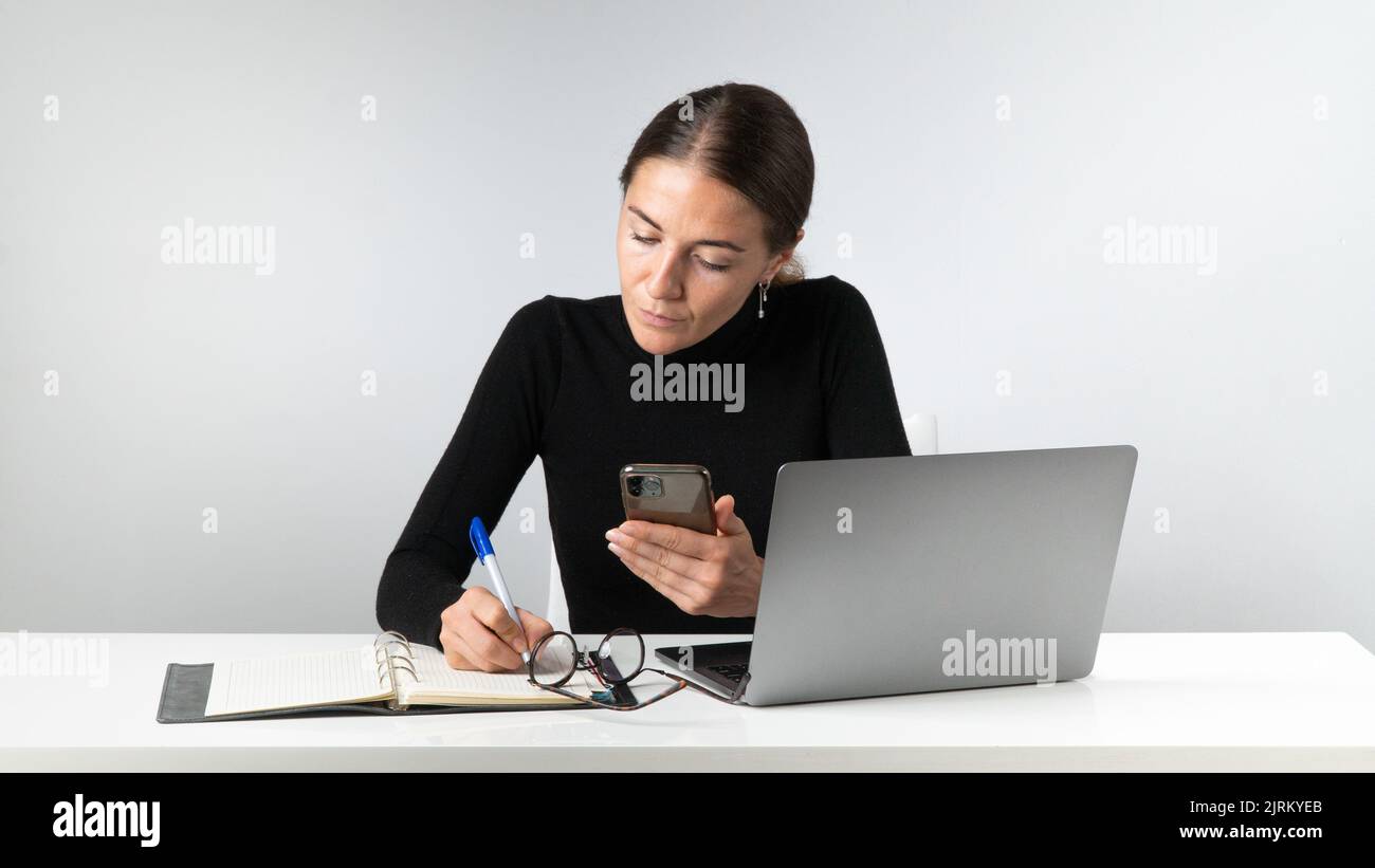 A woman works at a laptop, makes notes in a notebook, planning, routine ...