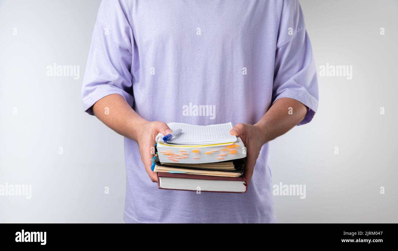 Male student holds a stack of notebooks and books on a white background ...