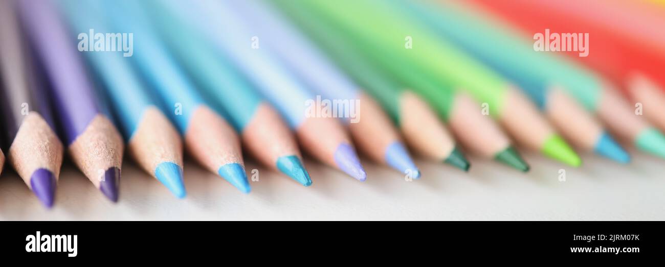 Many sharp multicolored pencils lying over colors of rainbow closeup ...