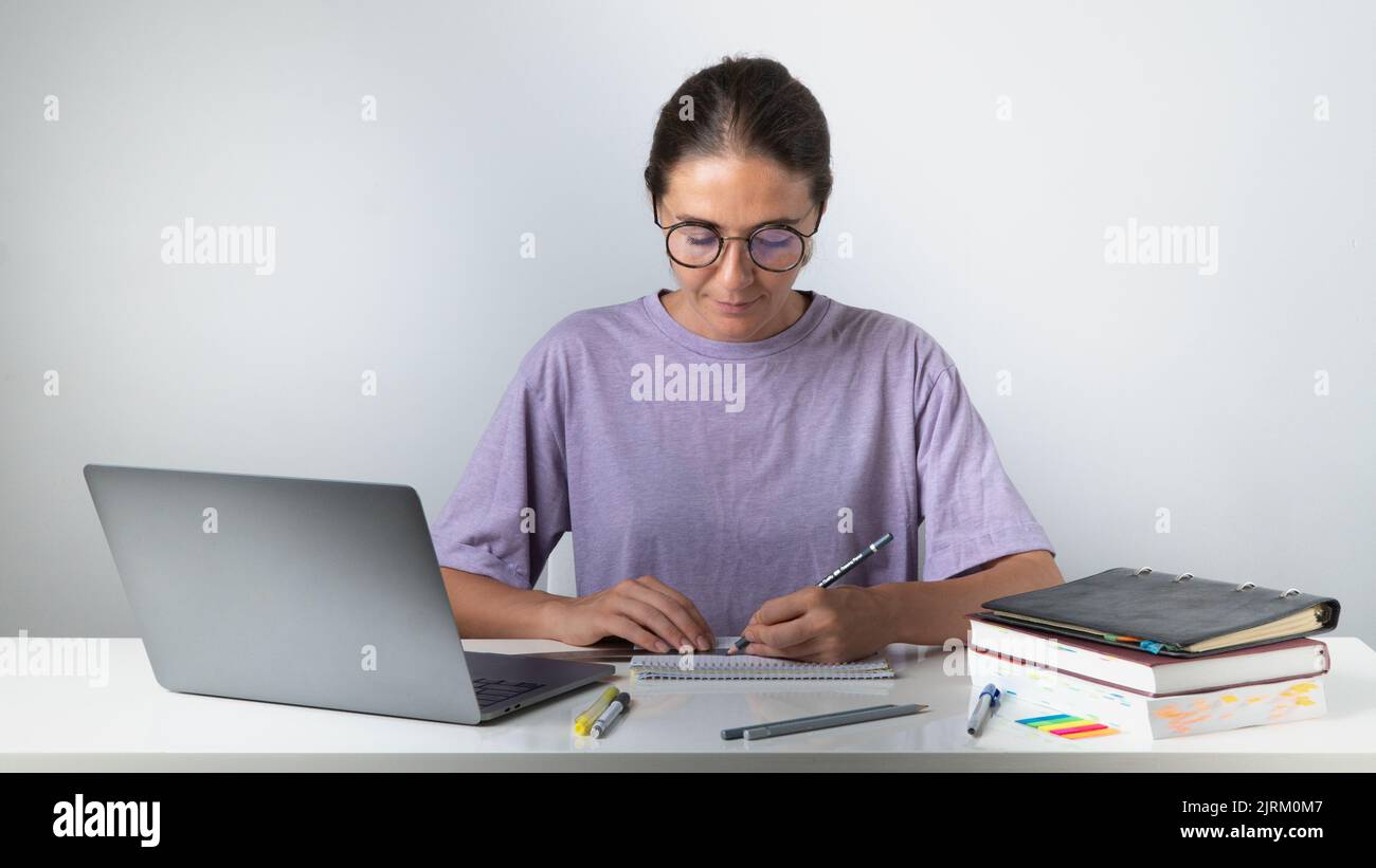 The student draws with a pencil and a ruler, on the table a laptop ...