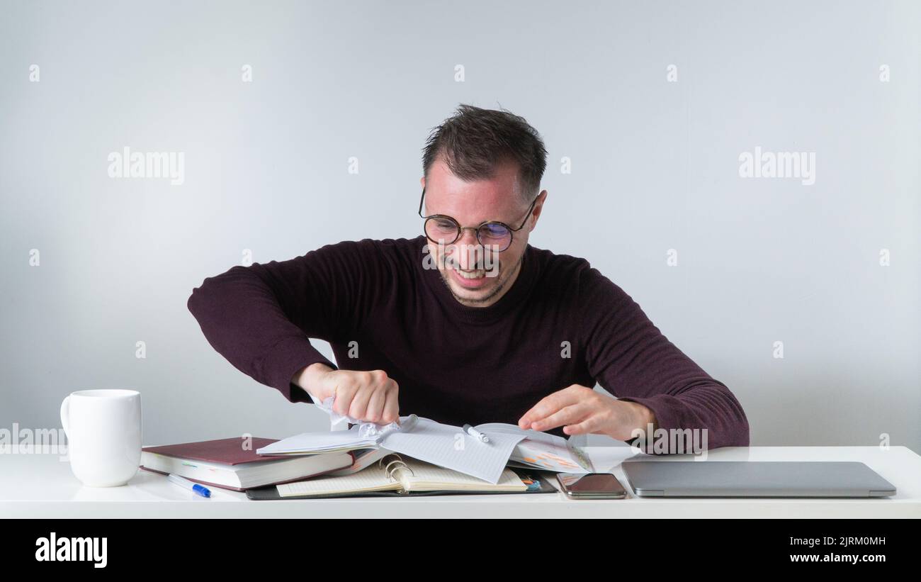 Angry man working in office tears out a piece of paper from a notebook ...