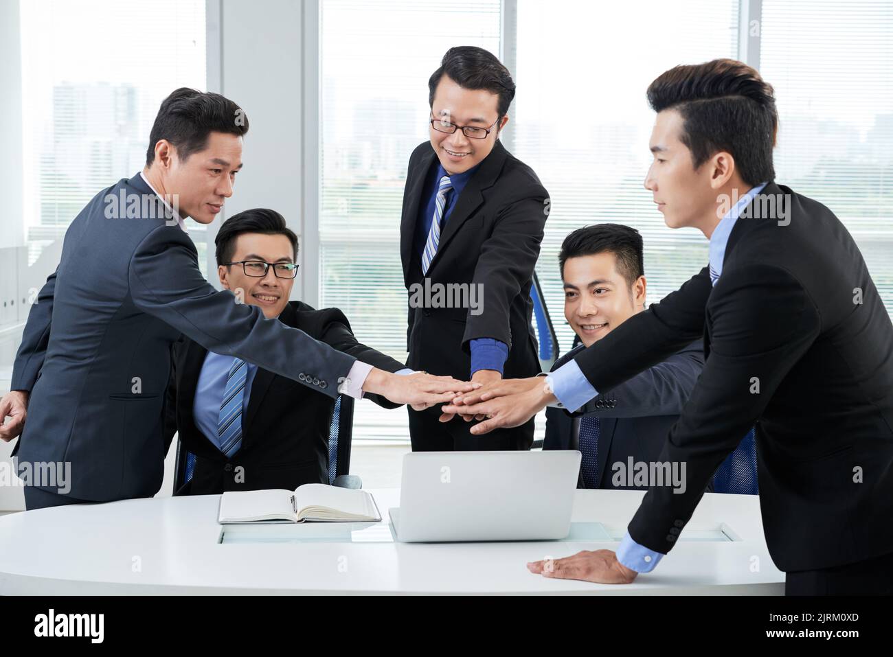 Ambitious team of white collar workers joining hands together while ...