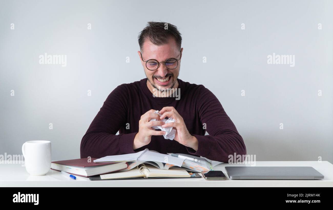 Angry employee man crumples paper into a lump in the office at the desk ...
