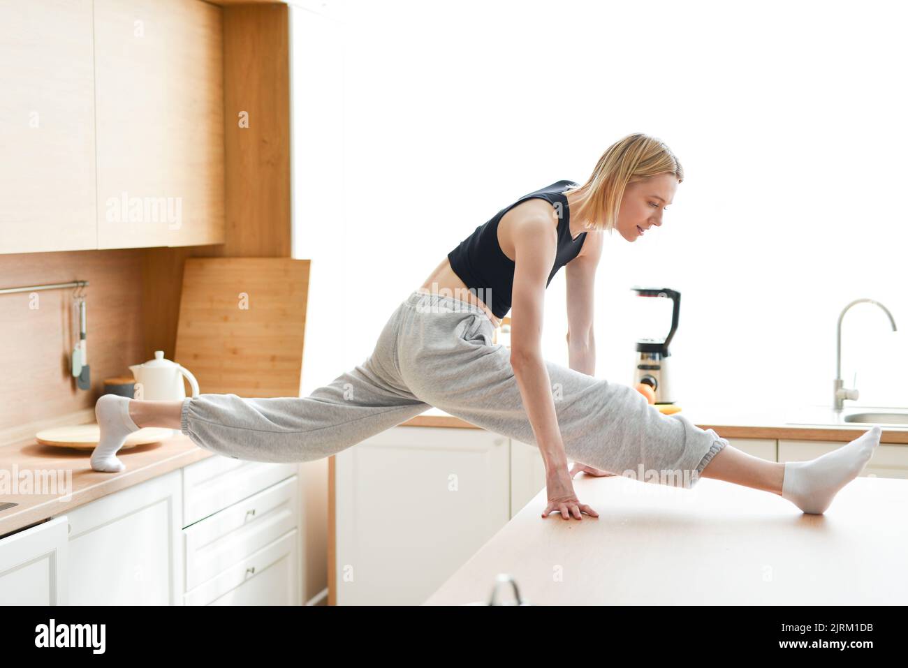 Woman doing the splits in kitchen between tables Stock Photo - Alamy