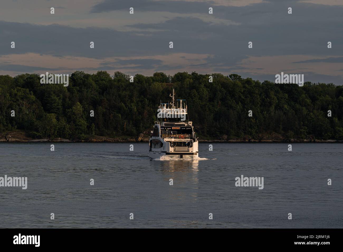 A small cruise ship in the water with a background of a forest Stock ...