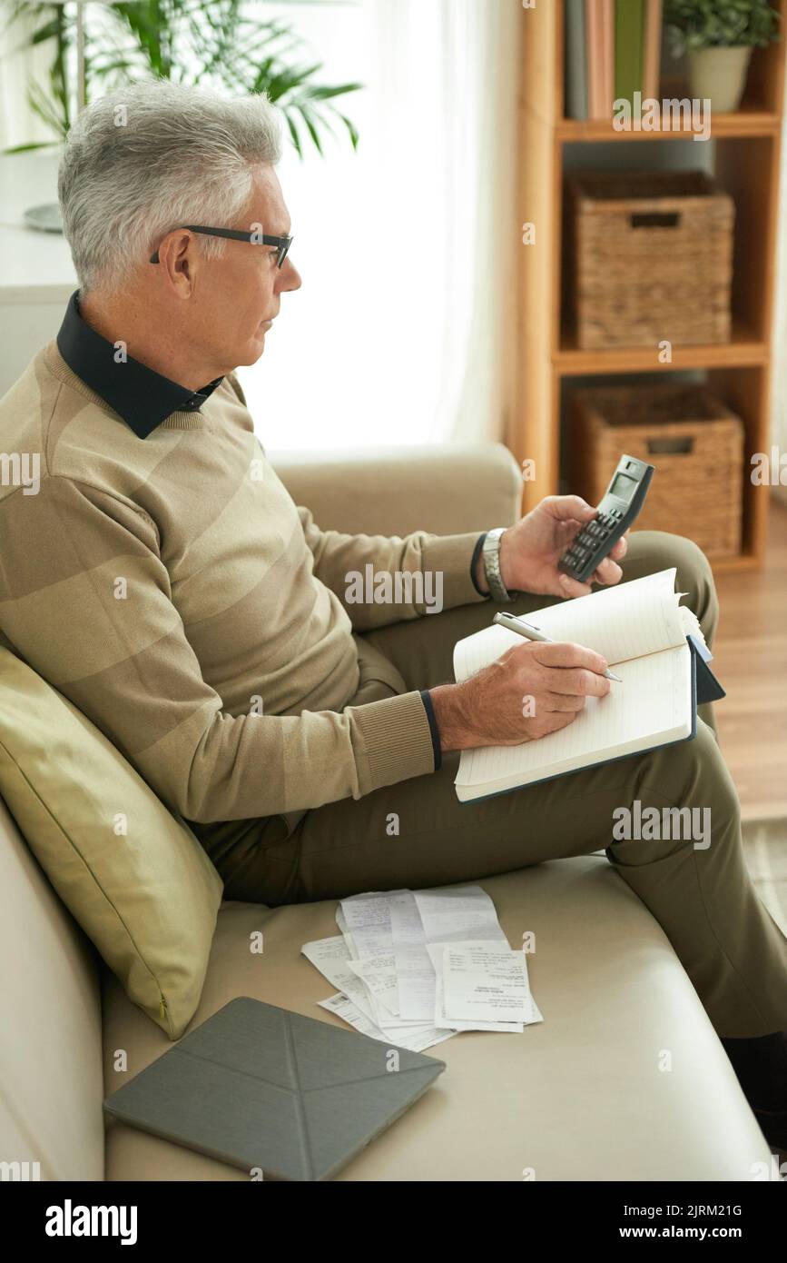 Senior man calculating expenses and writing figures in notepad Stock Photo - Alamy