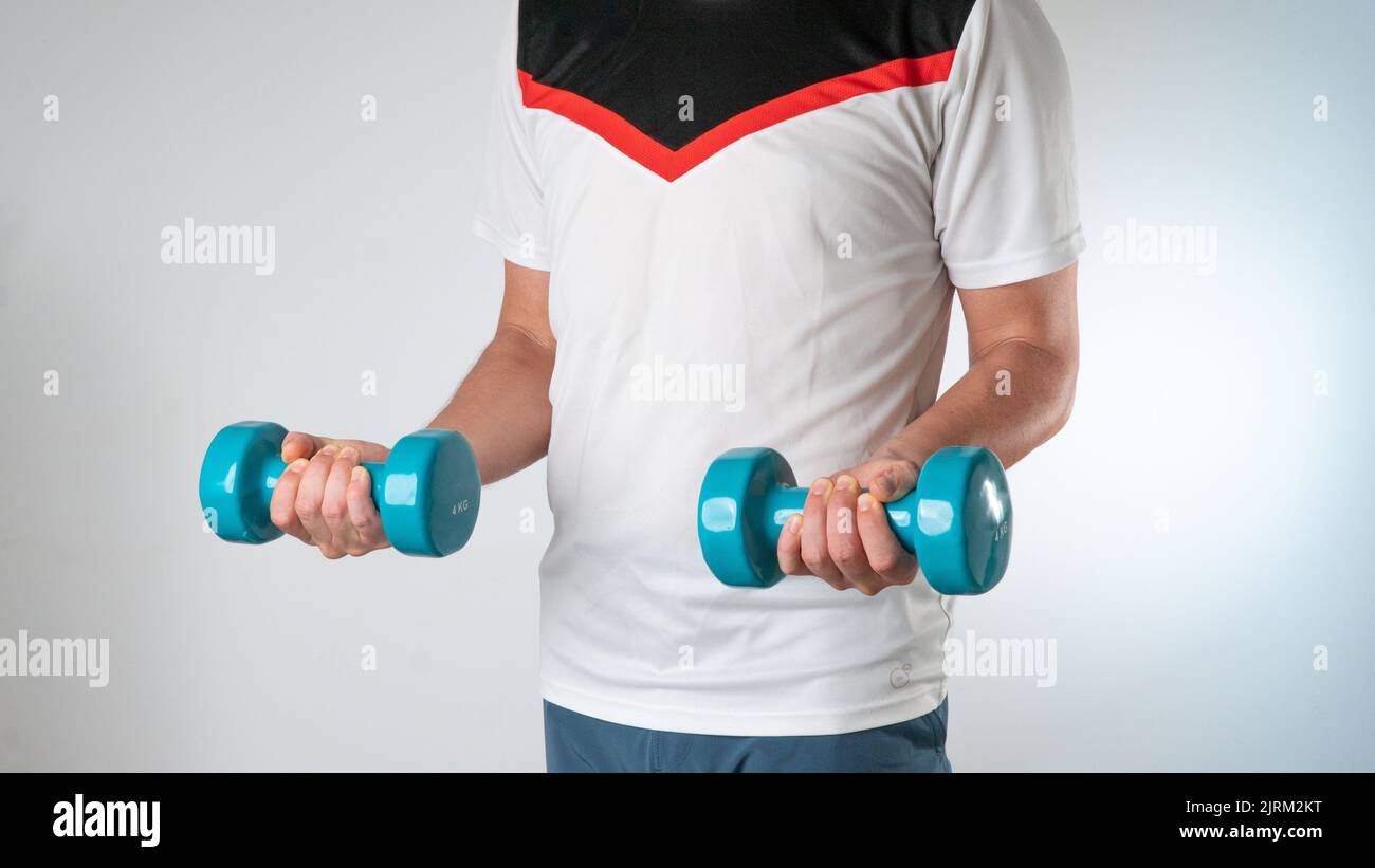 A sporty man with dumbbells in his hands does a workout to pump the ...