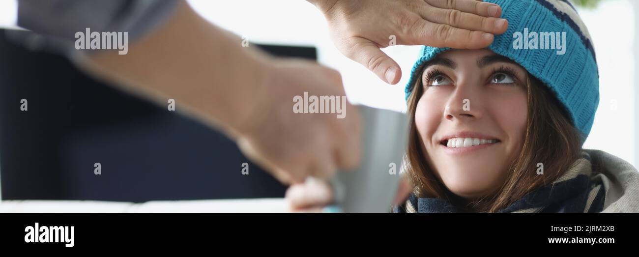 Man hand touching forehead of sick woman in hat and giving cup of tea ...
