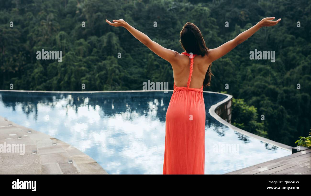 Rear view of young woman in sundress with hands raised standing at ...