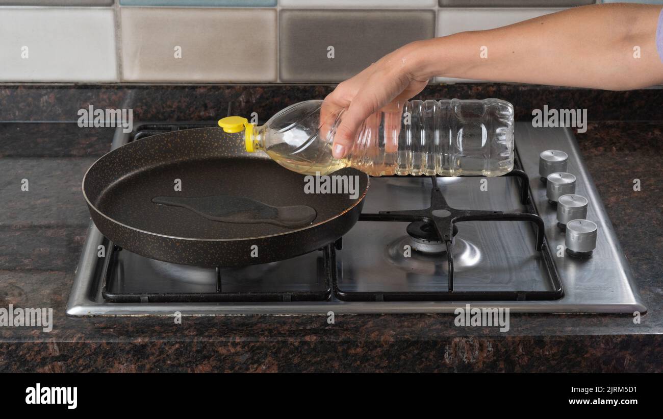 A woman's hand pours vegetable oil into a frying pan on the stove Stock ...