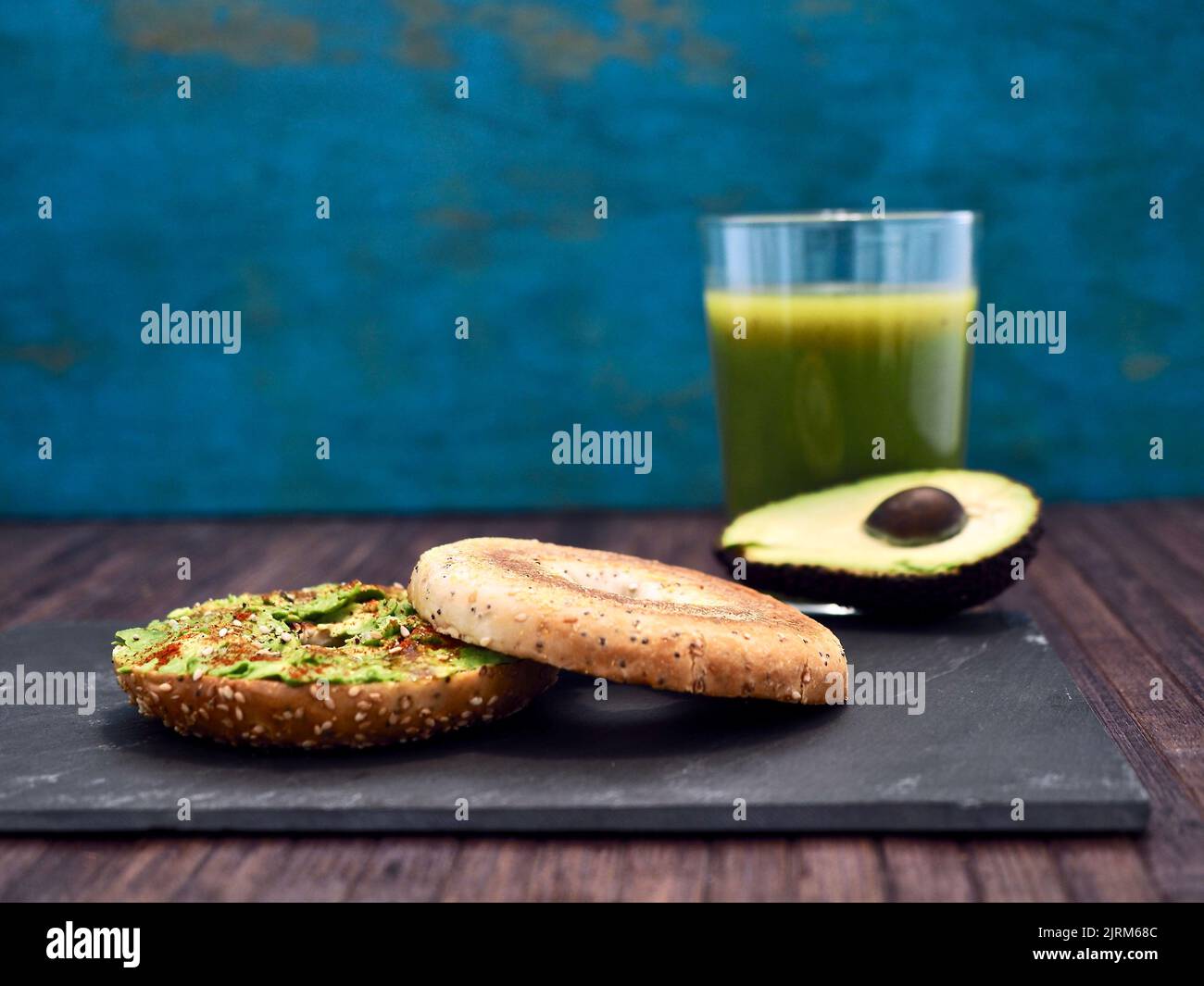 A closeup of avocado bagel and green smoothie in the background Stock ...