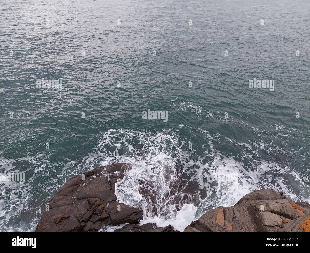 A high angle shot of a sea crashing on the shore cliffs with waves ...