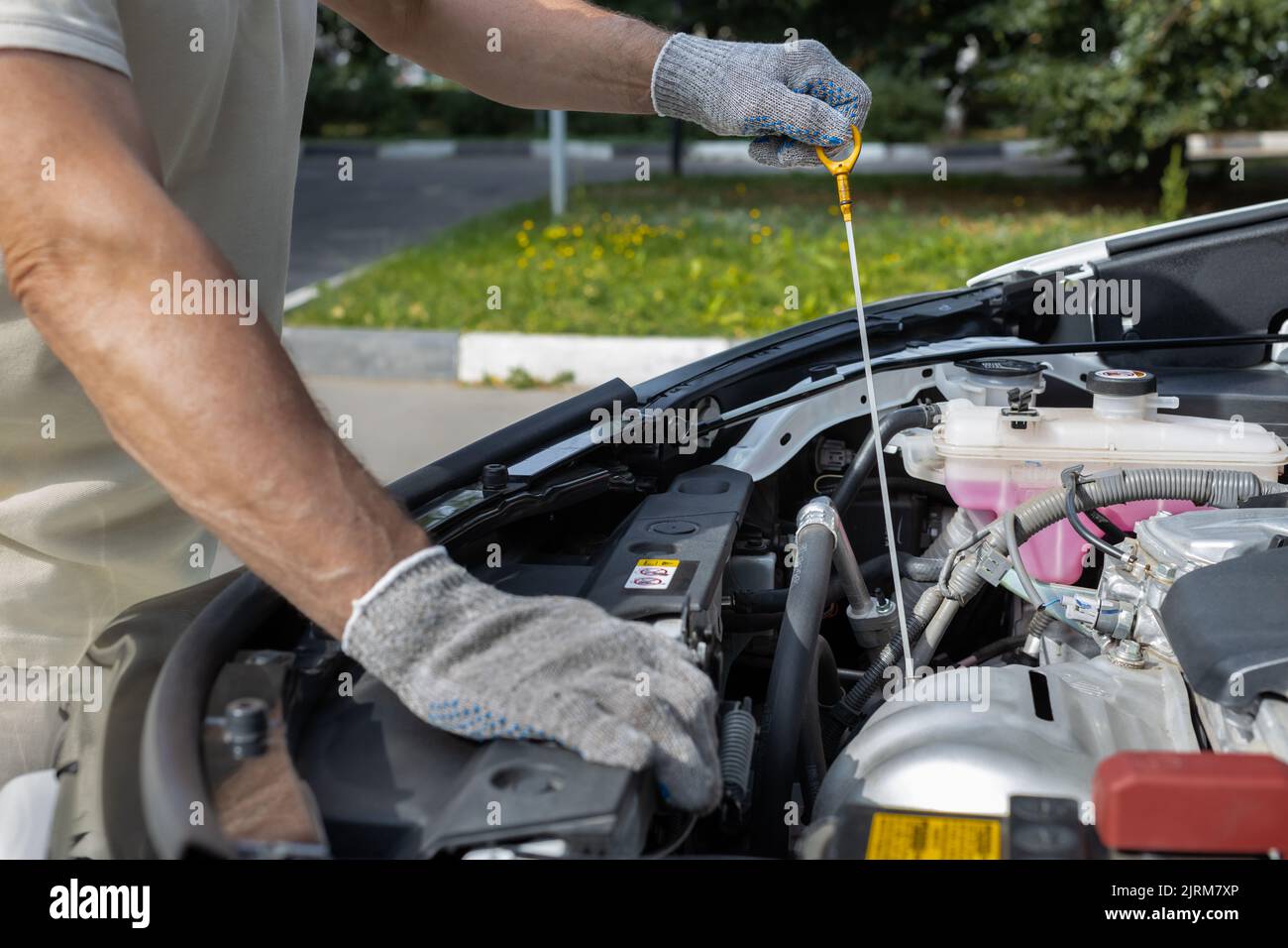 a man checks the oil level in a car engine. the hand takes out the dipstick to check the oil ...