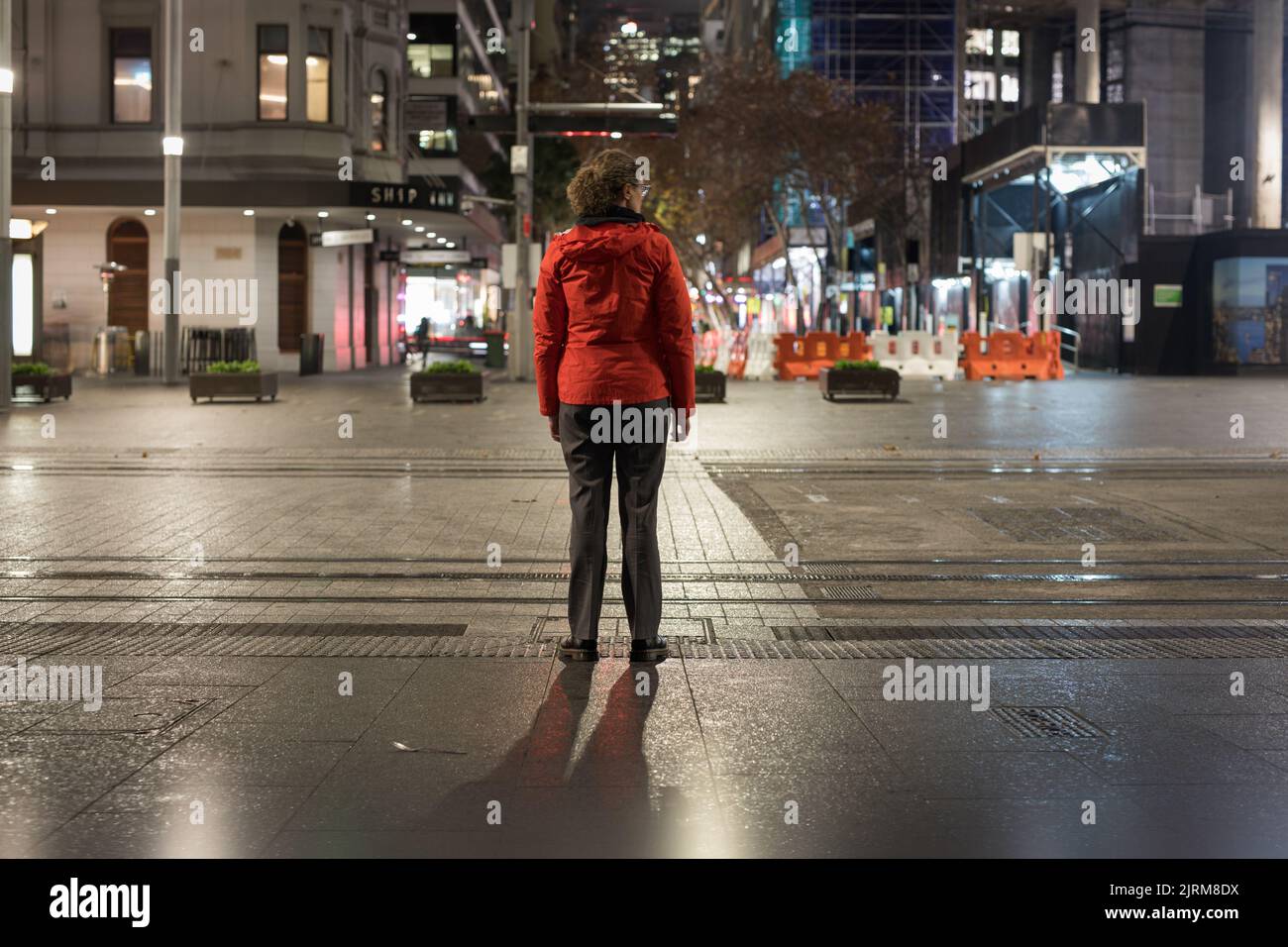 A female in a red coat facing the street on a rainy evening in downtown ...