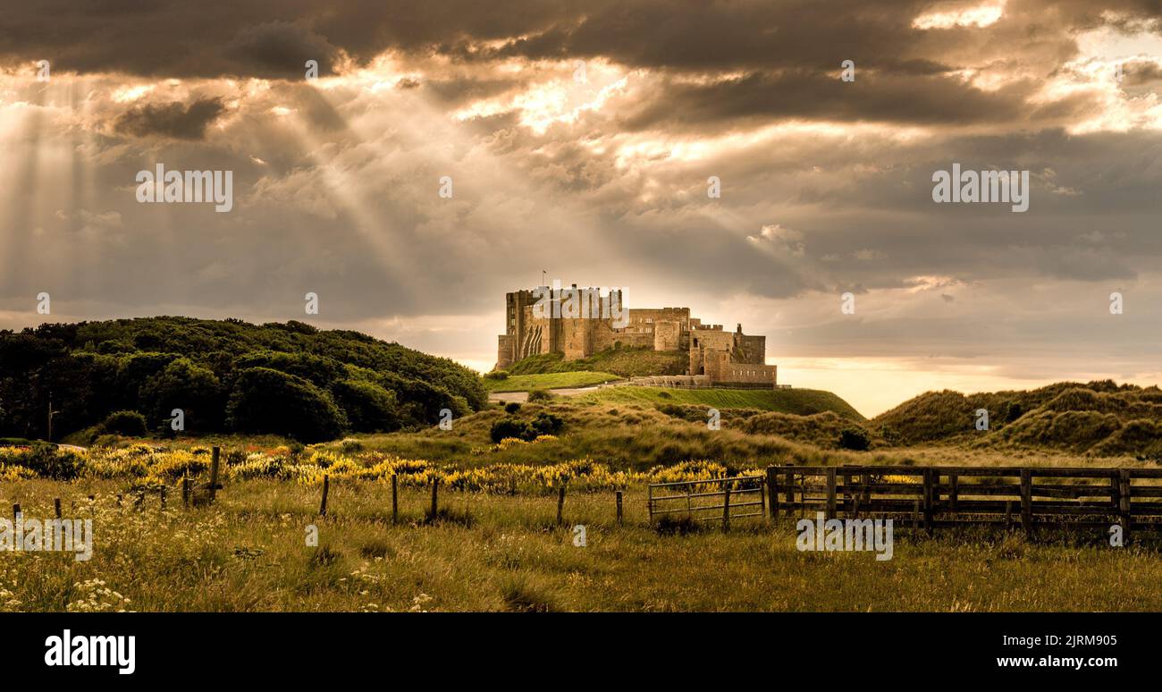 A dramatic shot of the Bamburgh Castle with sunlight peeking through ...