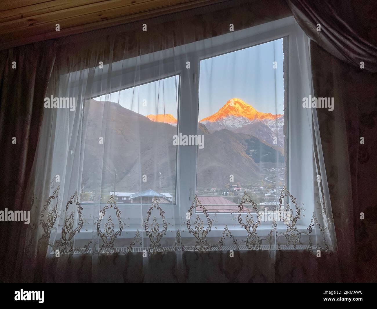 Breathtaking view of sunlit mountain Kazbegi ridge through window with ...