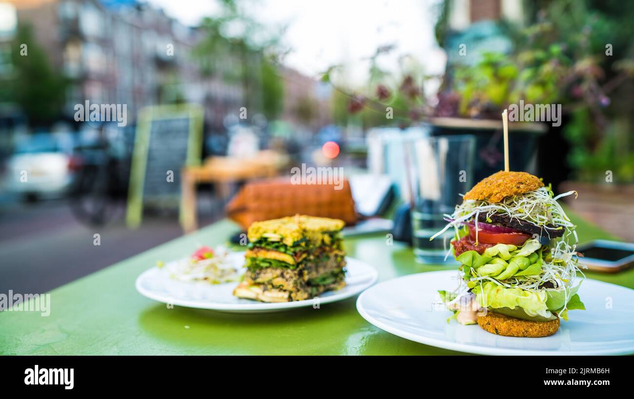 Two healthy vegan burgers on a green table at an outdoor seating cafe ...