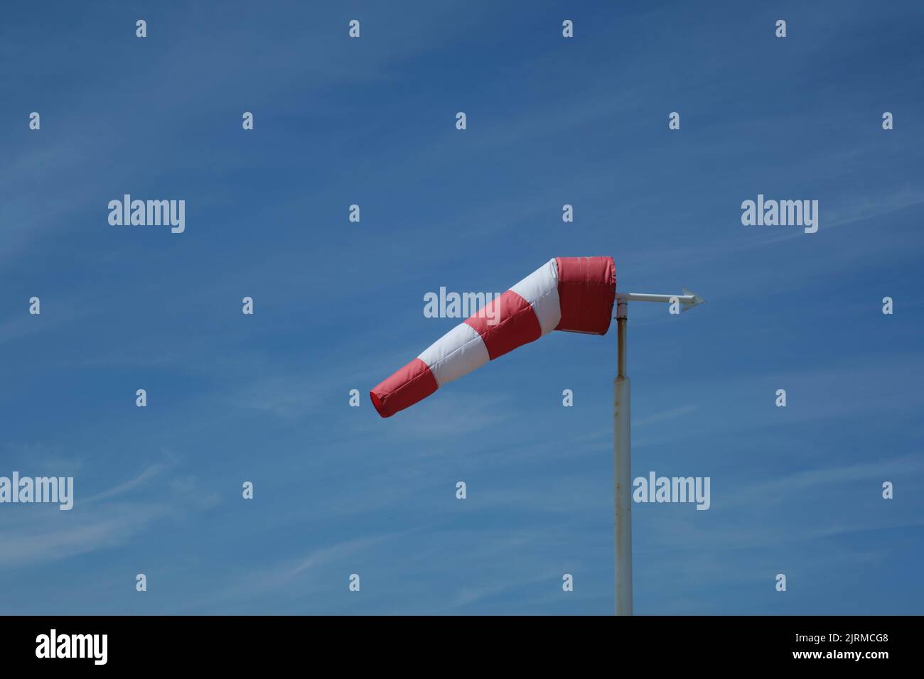 Red-white windsock against the blue sky in sunny weather. Wind vane ...
