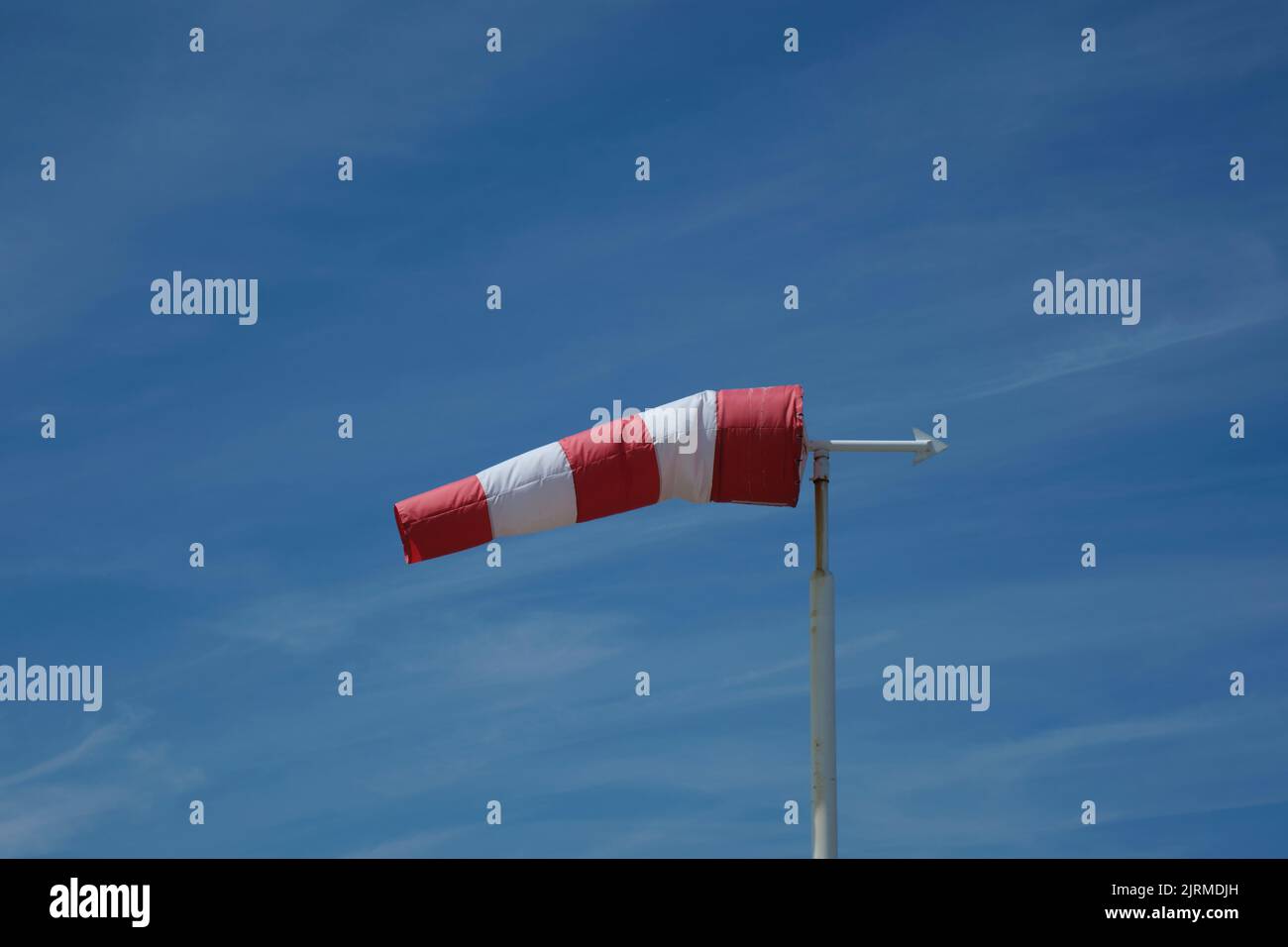 Red-white windsock against the blue sky in sunny weather. Wind vane ...