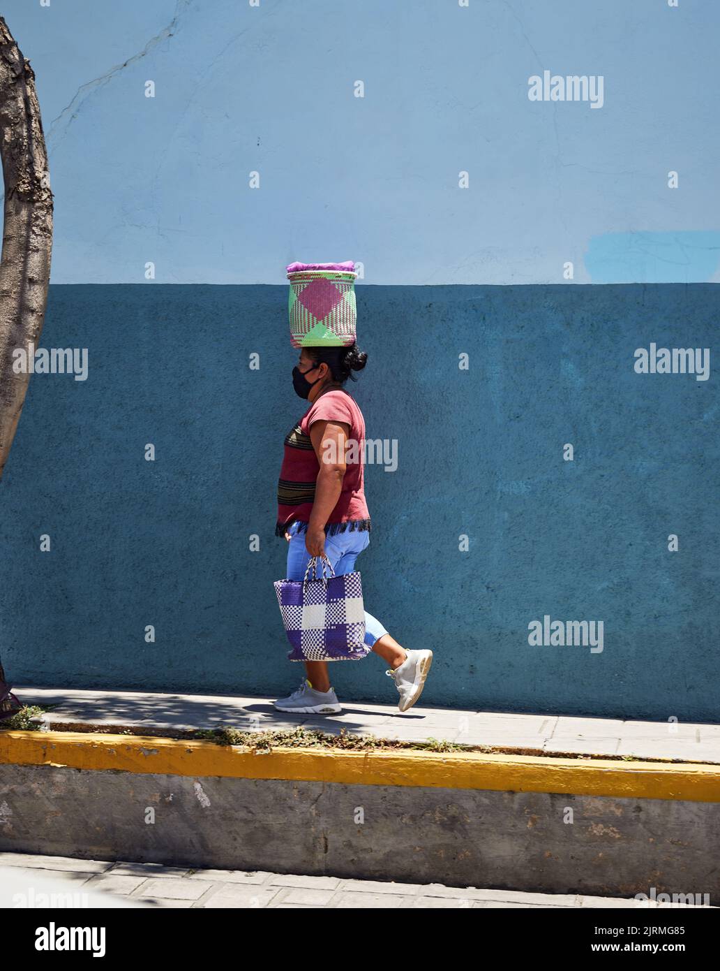 The vertical view of a woman walking on the sidewalk carrying the load ...