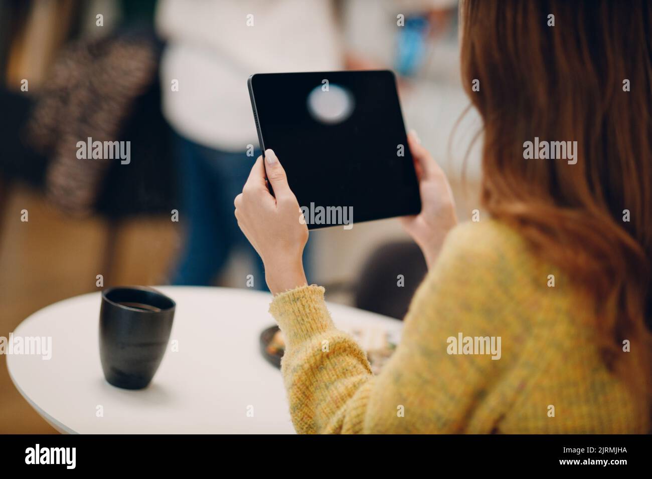 Beautiful young woman using digital tablet at cafe table with cup of ...