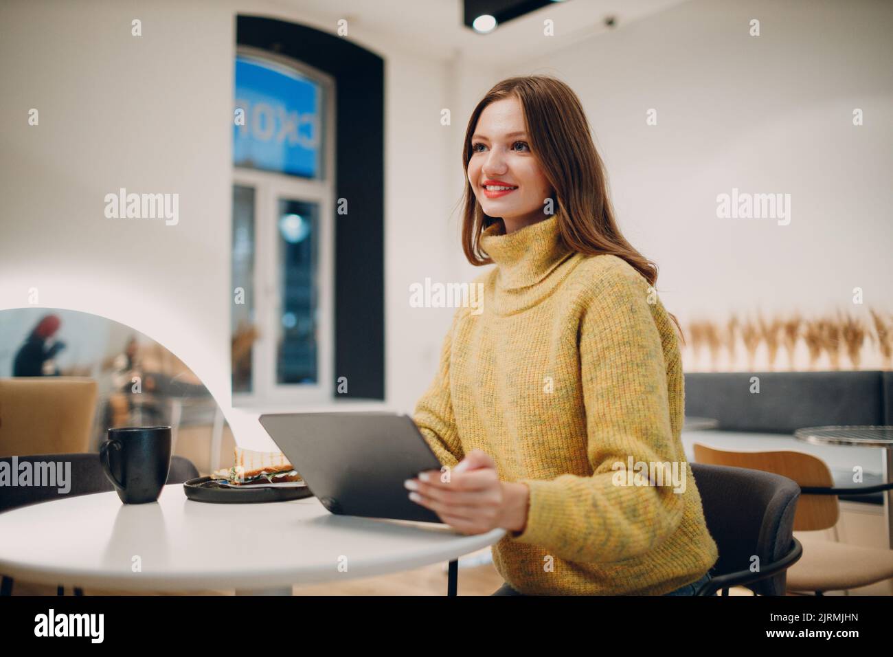 Beautiful young woman using digital tablet at cafe table with cup of ...