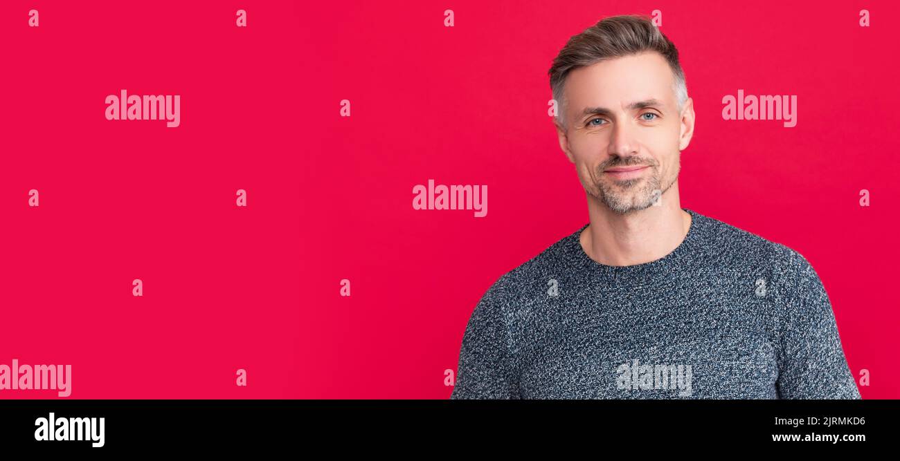 Man face portrait, banner with copy space. positive grizzled guy in sweater on red background ...