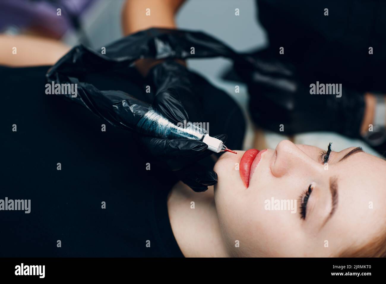 Cosmetologist applying red permanent make up tattoo on young woman lips ...