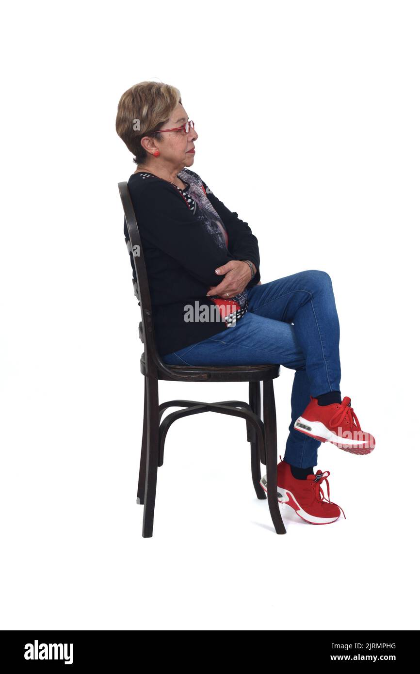 side view of a full portrait of serious woman sitting on chair on white ...